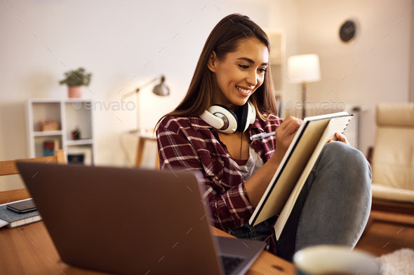 Happy student writing in her notebook while learning online at home ...