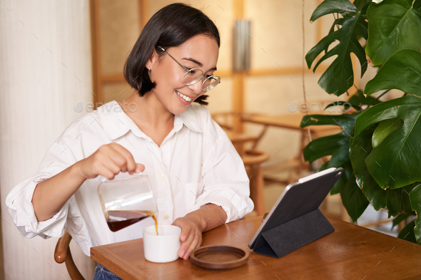 Freelance and remote workers. Smiling young woman pouring coffee in a ...