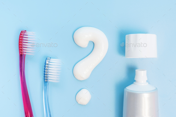Toothbrushes, toothpaste and question mark on blue background close-up ...
