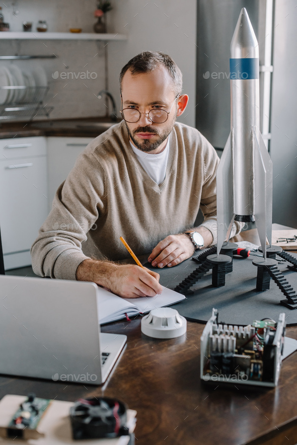 handsome engineer modeling rocket, looking at laptop and making notes ...