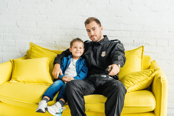 young father in police uniform watching tv with son while sitting on ...