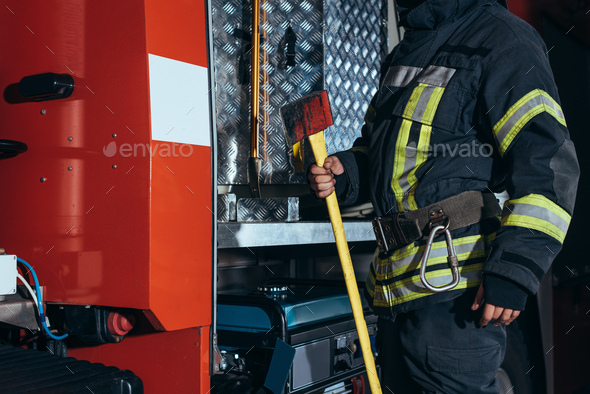 partial view of firefighter in fireproof uniform holding axe at fire ...