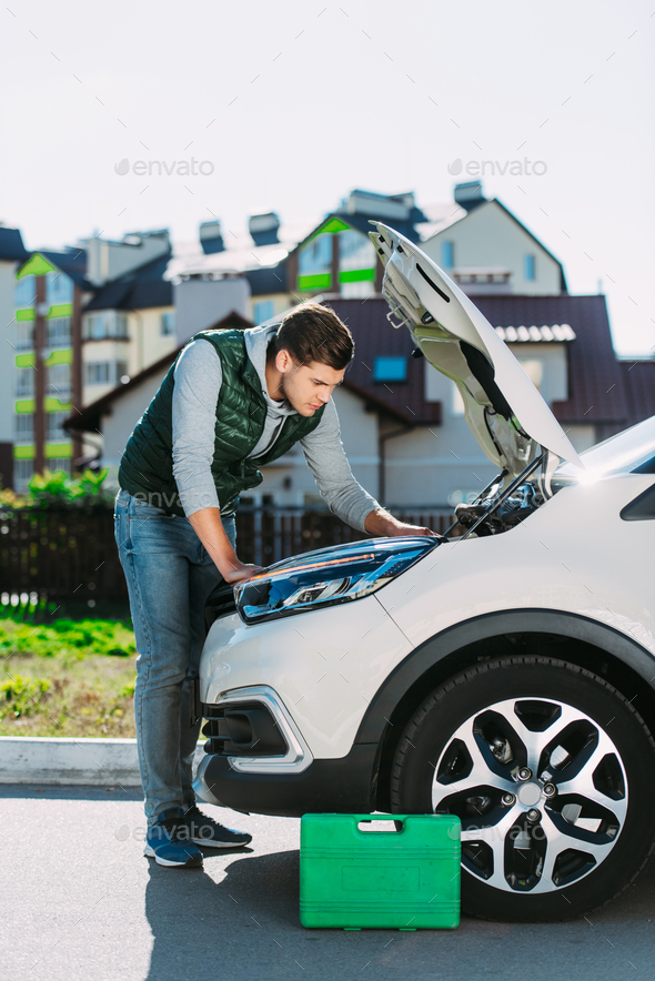side view of focused young man repairing broken car on street Stock ...