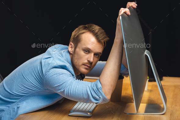 overworked young businessman holding computer monitor and looking at ...