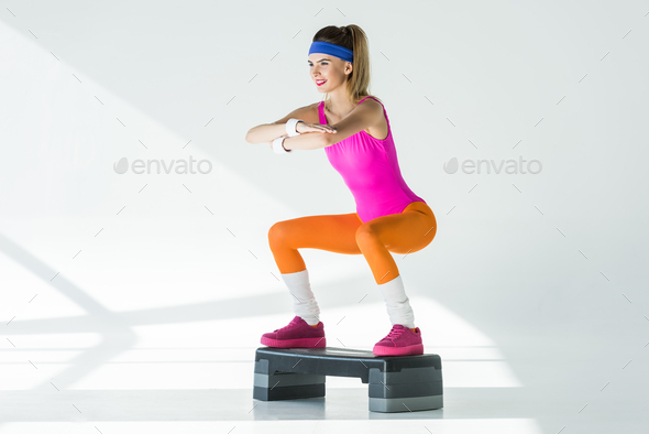 athletic young woman doing squats on step platform and looking away on ...