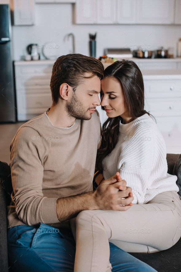 beautiful young couple cuddling and holding hands on couch at home ...