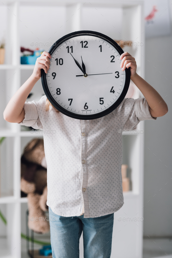 little child covering face with big clock Stock Photo by LightFieldStudios