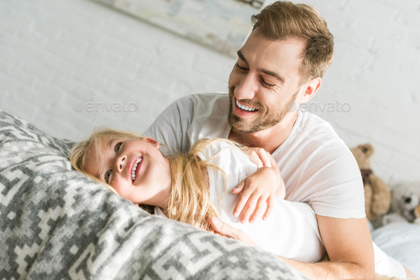 happy father hugging adorable little daughter on bed Stock Photo by LightFieldStudios