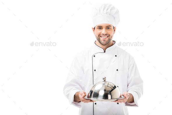smiling young chef holding serving tray with dome and looking at camera ...