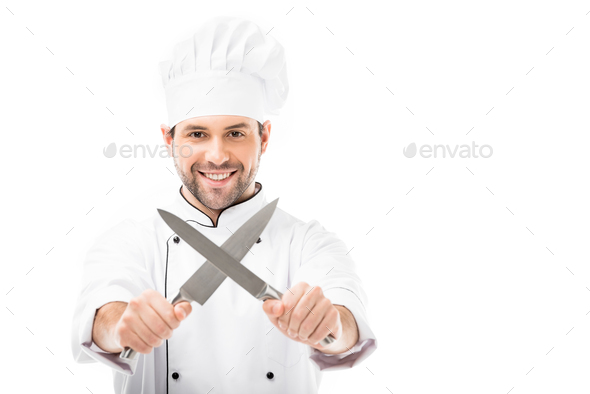 smiling young chef holding cutting knives in shape of x and looking at ...