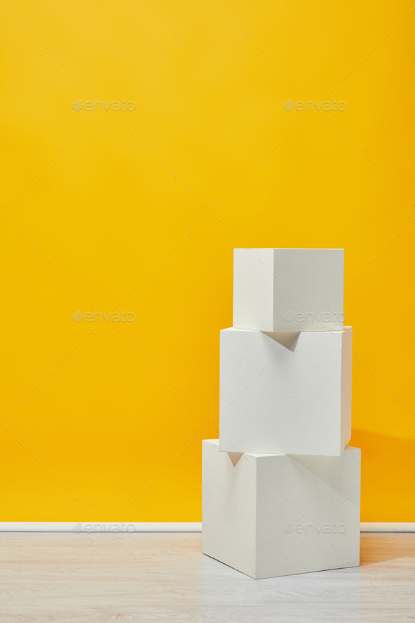 Minimalistic white plaster cubes arranged vertically near yellow wall ...