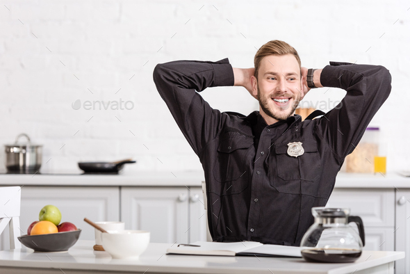 Smiling police officer with hands on head sitting at kitchen table ...