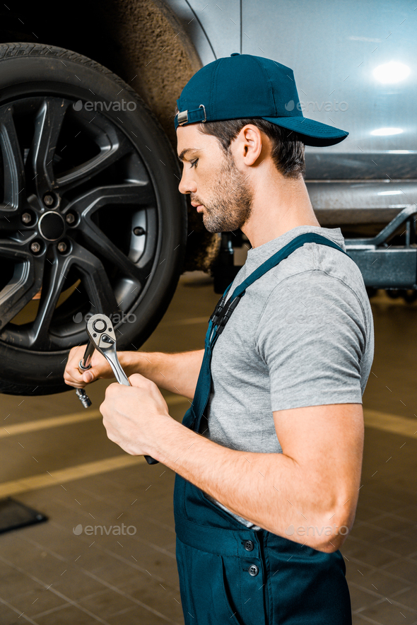 side view of male auto mechanic in working overall standing with wheel ...