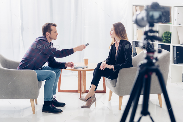 side view of businesswoman in suit giving interview to journalist with ...