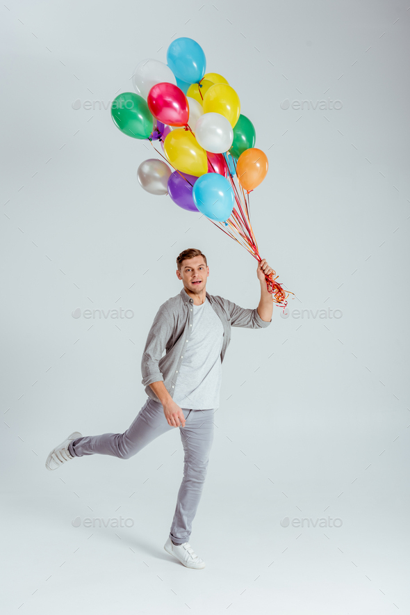 man jumping with bundle of colorful balloons and looking at camera on ...
