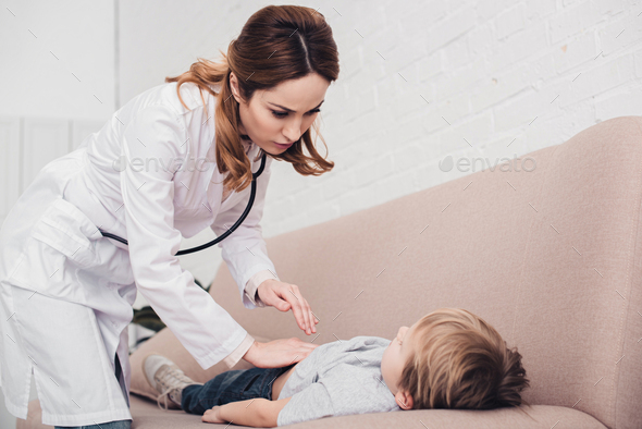 pediatrist palpating sick boy stomach on sofa in living room Stock ...