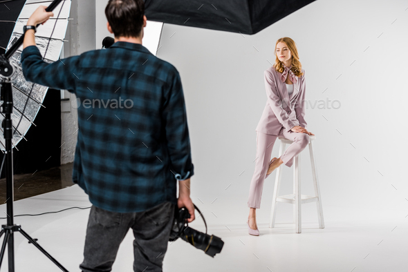 back view of photographer holding camera and model posing in studio ...