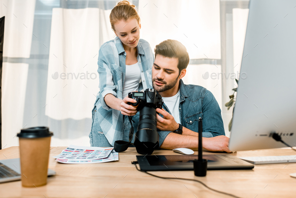 professional smiling young photographers using photo camera together in ...