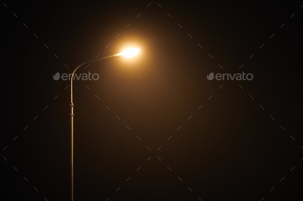 One night lamppost shines with faint mysterious yellow light through ...