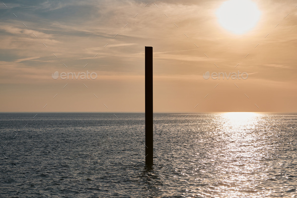 Large rusty steel construction pillar in blue sea with calm waves at ...