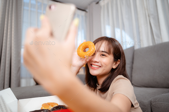 Young woman while watching TV, relaxing, eating snack and donut by ...
