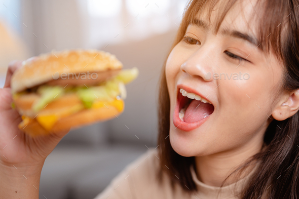 Hungry young woman eating junk food hamburger and pizza for lunch by ...