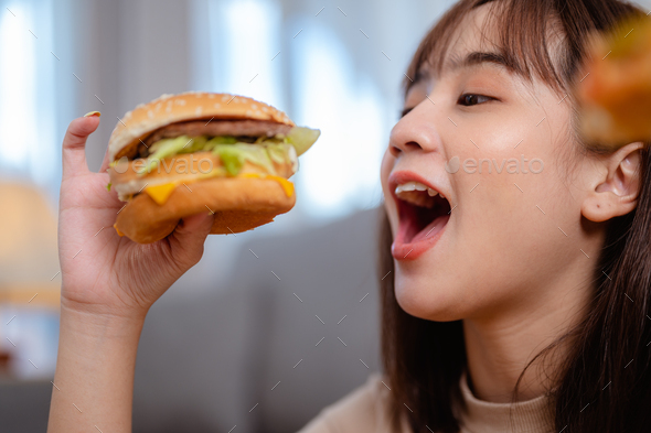 Hungry young woman eating junk food hamburger and pizza for lunch by ...