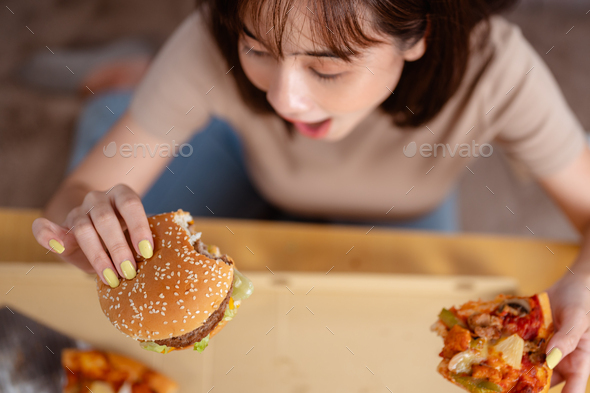 Hungry young woman eating junk food hamburger and pizza for lunch by ...