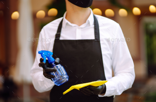 Disinfecting to prevent COVID-19. Waiter cleaning the table with ...