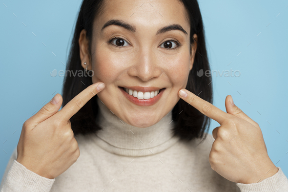 Portrait of pretty cheerful woman points index fingers at smile shows ...