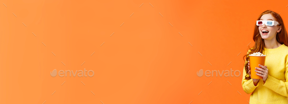 Girl eating popcorn, smiling amused as staring at large screen watching ...