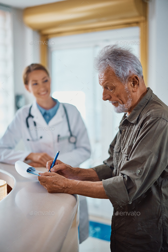 Senior man filling medical paperwork at reception desk at doctor's ...