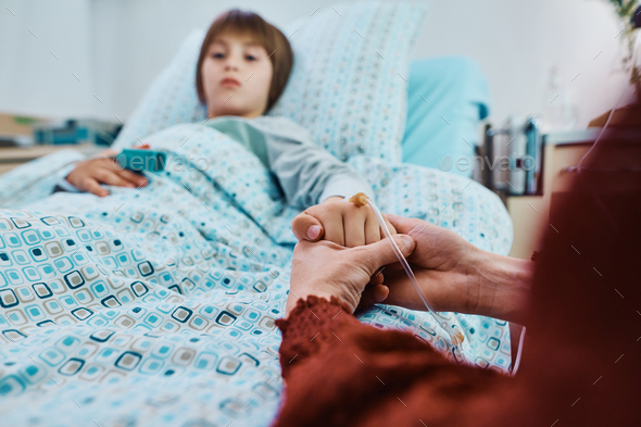 Close up of mother holding hand of her son who is recovering at ...
