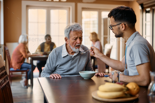 Old man eating with help of caregiver during lunch time at nursing home ...