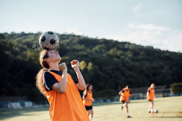 Skillful female soccer player balancing ball on the head on playing ...
