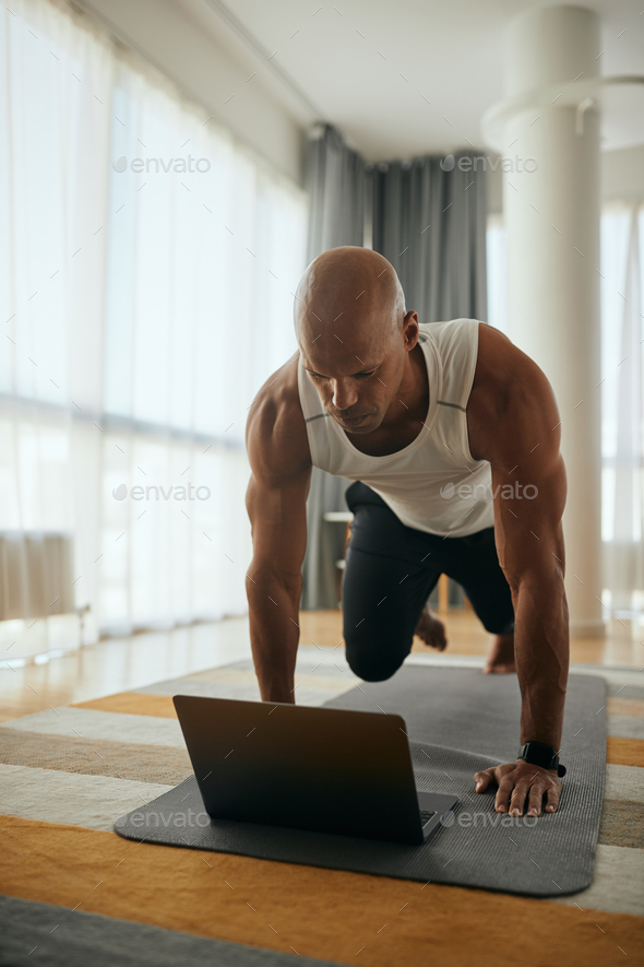 Young black athlete following online exercise class over laptop while ...