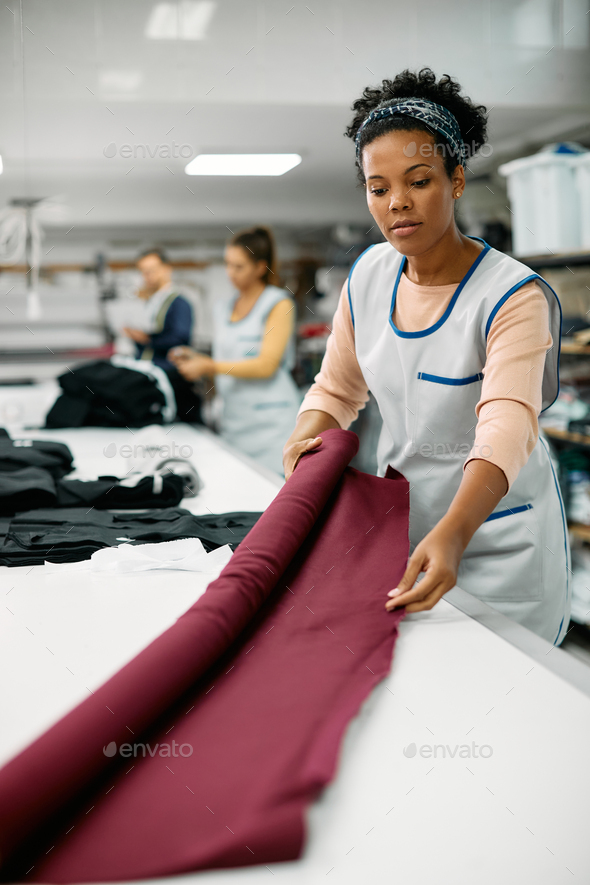 Black female textile worker using new fabric roll while working at ...