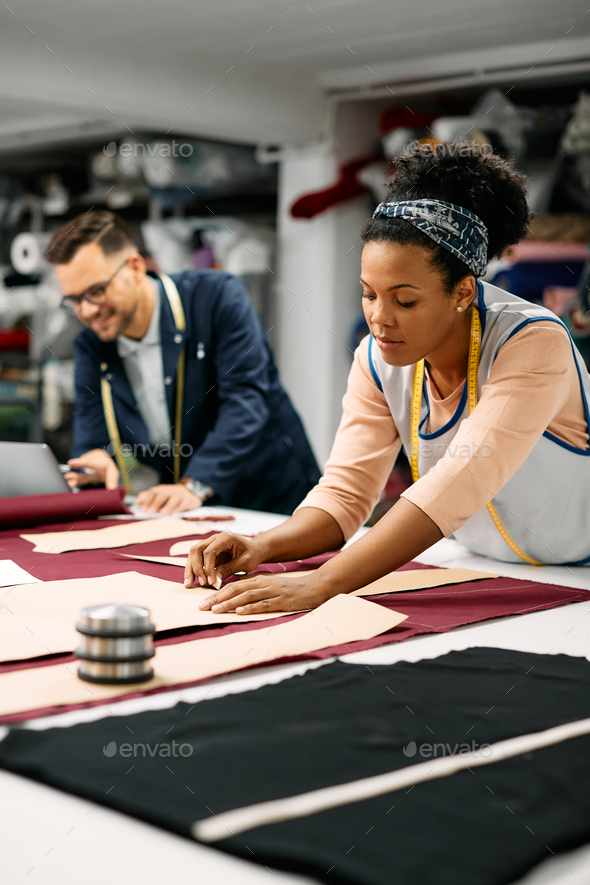 African American textile worker marking fabric with chalk at tailor's ...