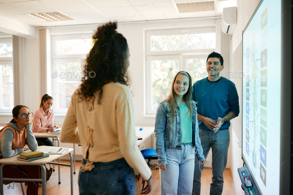 High school students and their teacher talking while using smartboard ...