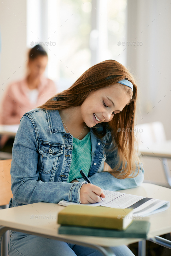 Happy teenage girl taking notes while learning during a class at high ...