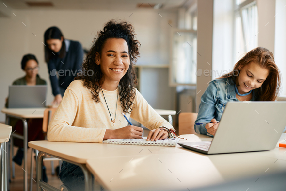Happy black student taking notes while using laptop with her classmate ...