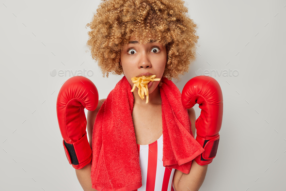 Shocked curly female boxer poses with mouth full of crisps wears ...