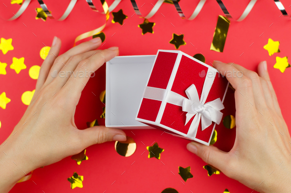 Open gift box in female hands on a red festive background, close-up ...