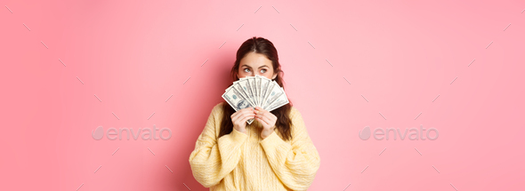 Beautiful young woman hiding face behind dollar bills, holding money ...