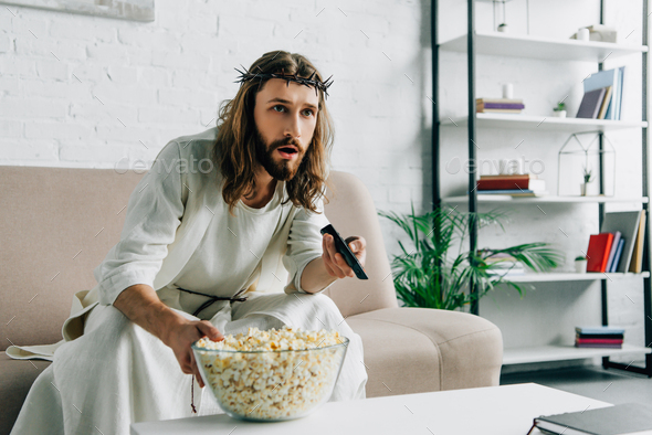 shocked Jesus in crown of thorns watching tv and sitting with bowl of ...