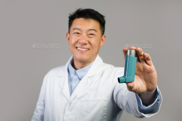 Smiling mature chinese male therapist in white coat showing inhaler for ...