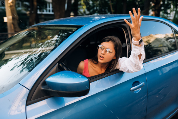 A young angry woman peeks out of the car window Stock Photo by simbiothy