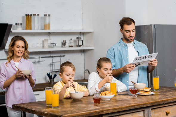 son and daughter eating oatmeal while father reading travel newspaper ...