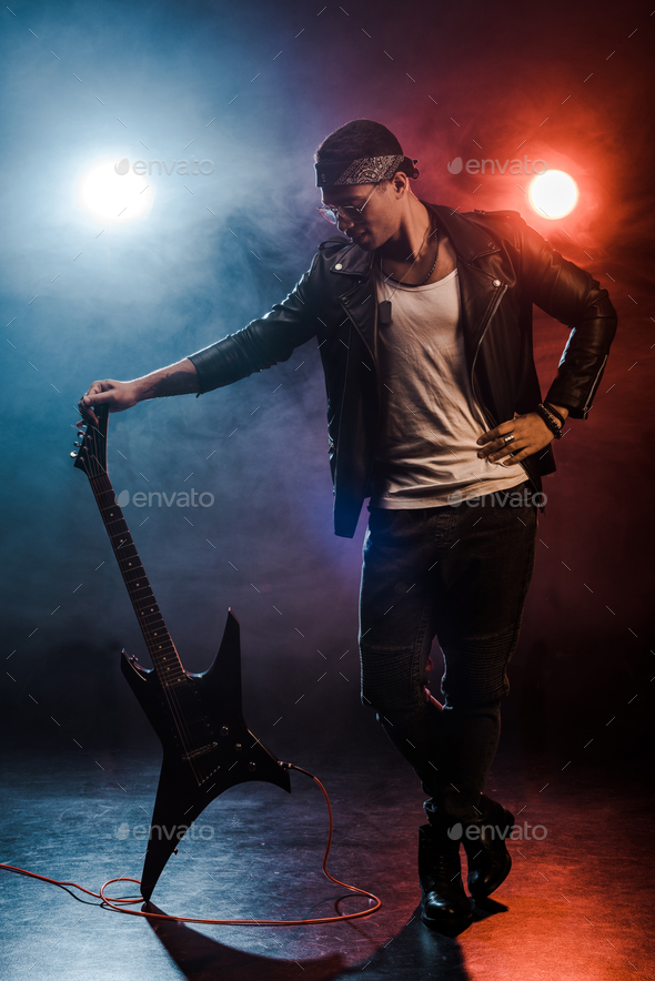young mixed race rock musician in leather jacket posing with electric ...