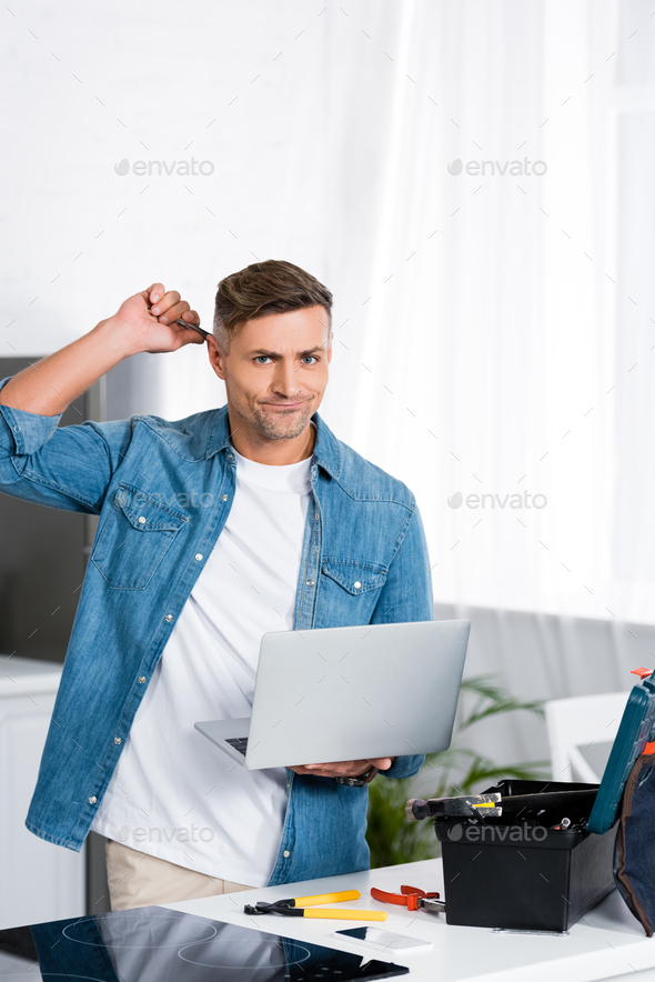 confused man holding laptop and scratching head with tool Stock Photo ...
